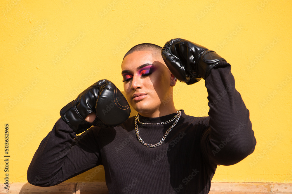 Young non-binary person wears boxing gloves on a mustard yellow ...