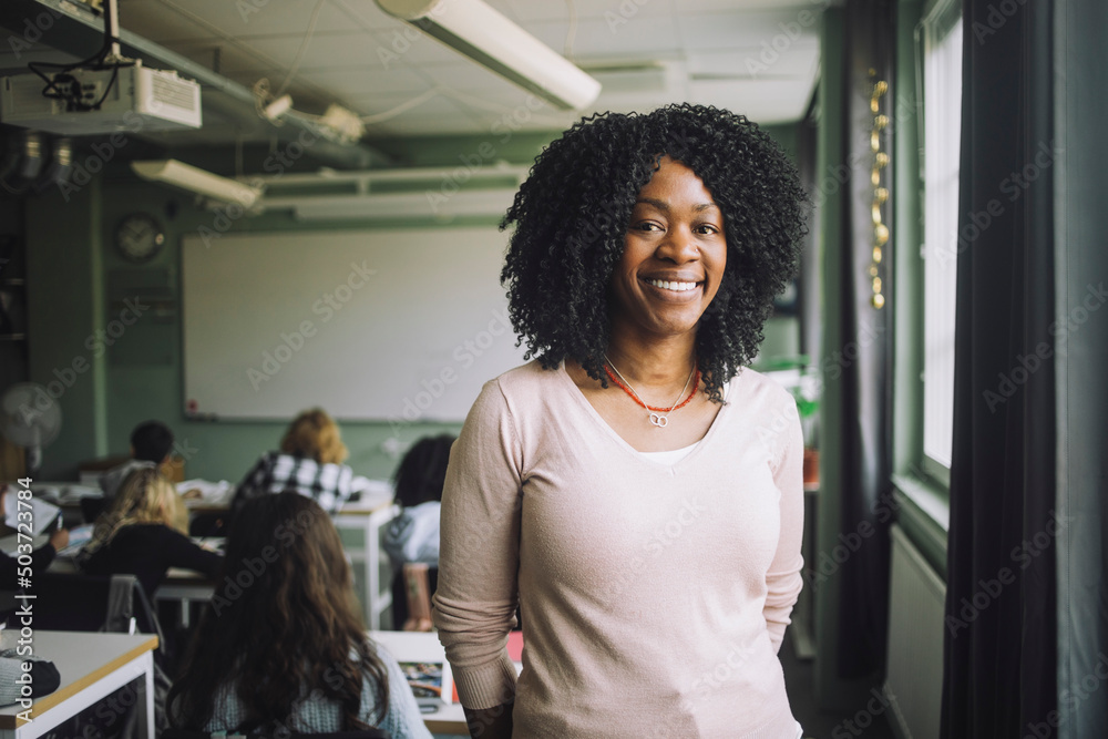 Smiling teacher with curly hair standing in classroom Stock Photo ...
