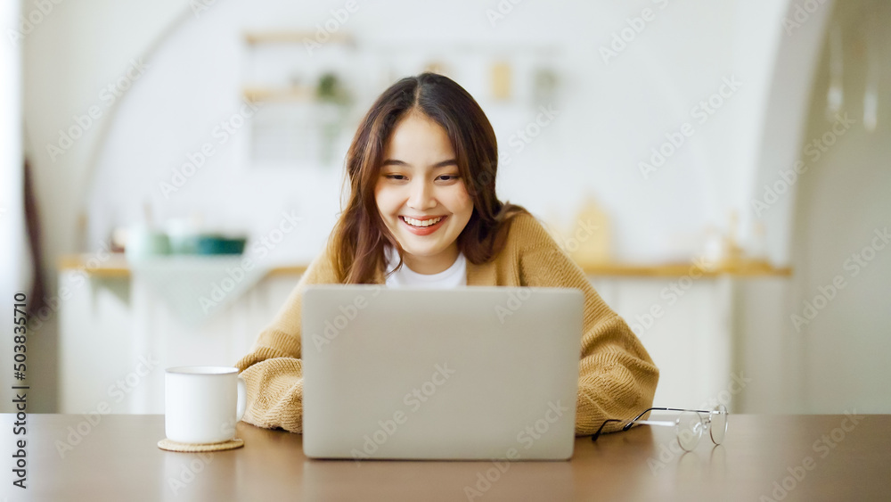 Smiling asian young woman working on laptop at home office. Young asian ...