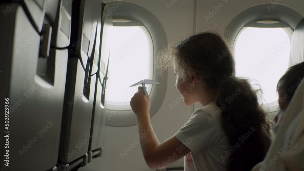 Child sitting by aircraft window and playing with little paper plane ...