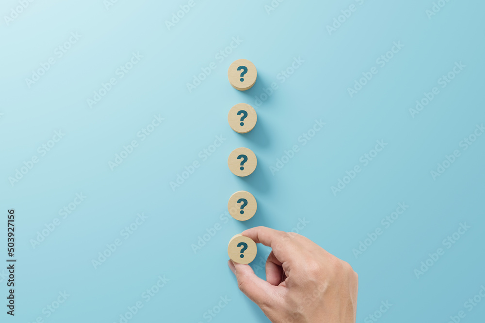 Hand holding wooden block shape with sign question mark symbol on blue ...