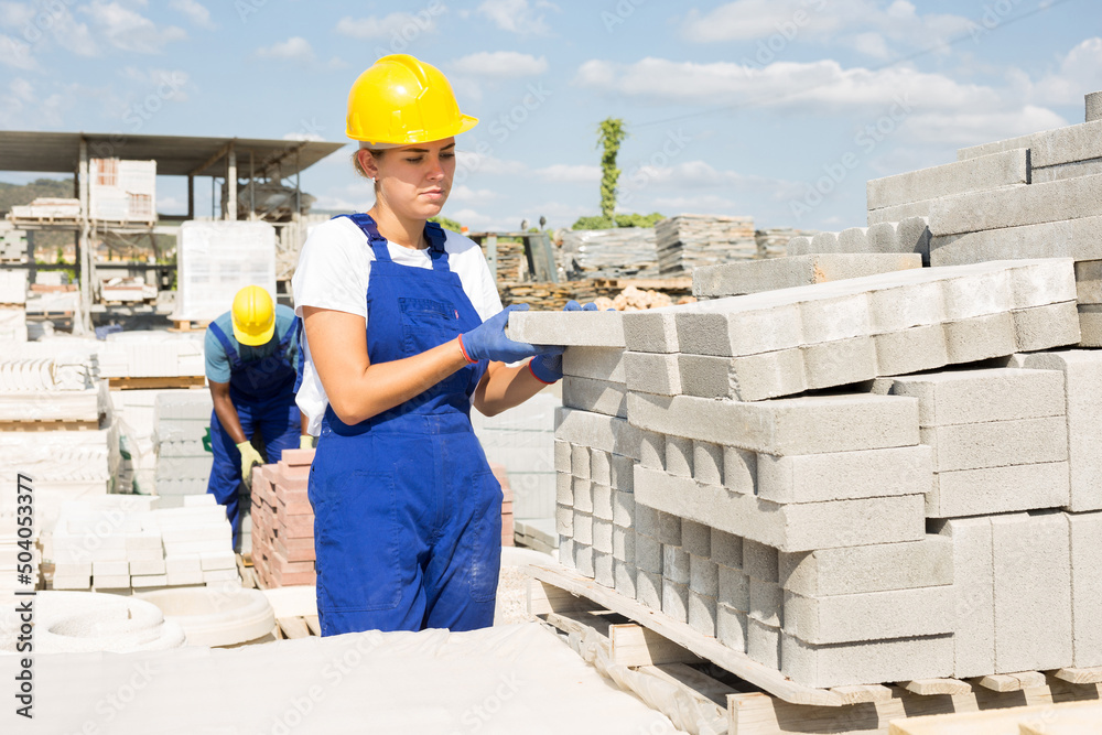 Female worker stacking paving slabs in warehouse of building materials ...