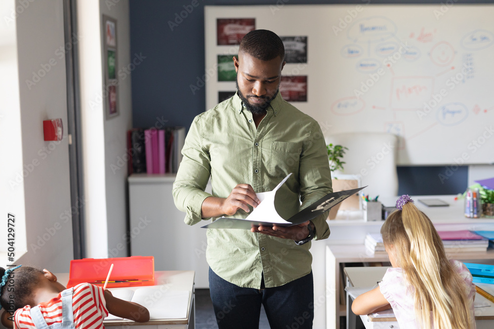 African american young male teacher reading file while standing by ...