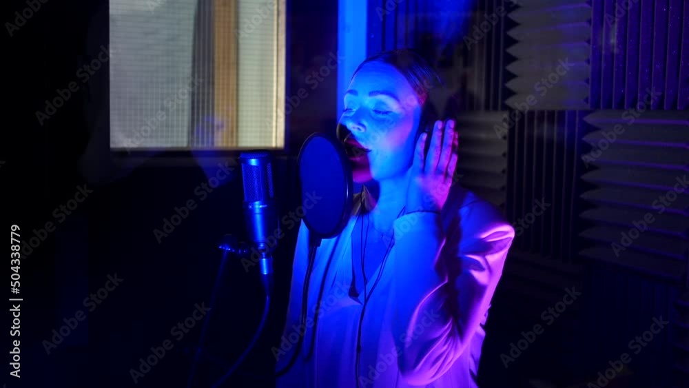 Tracking shot of a girl singing in a vocal booth through the recording ...