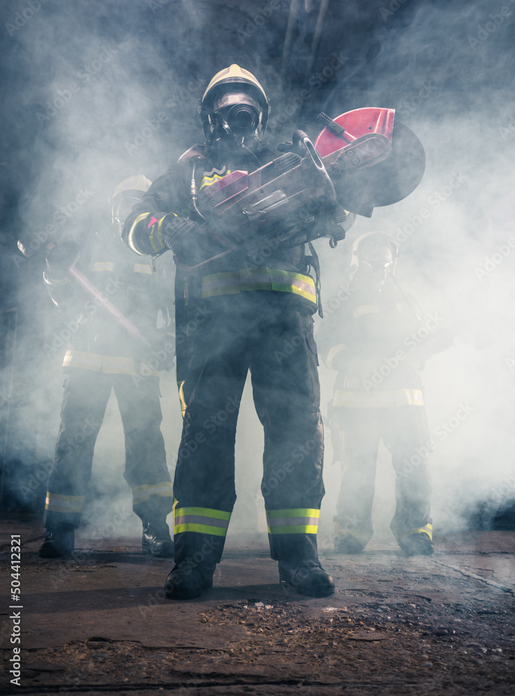 Portrait of fireman holding a rescue chainsaw in smoky garage of the ...