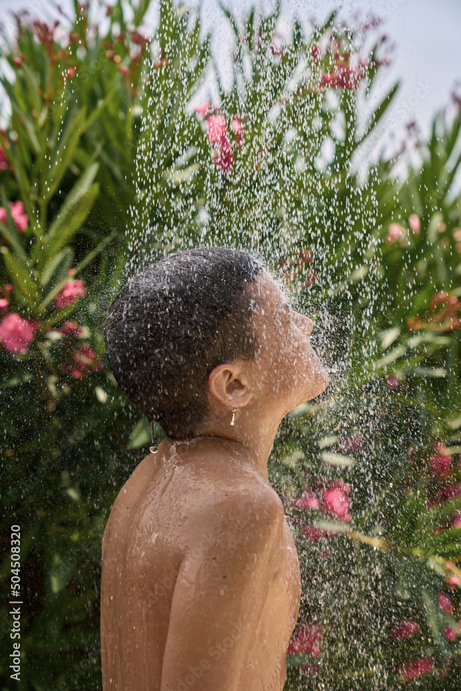 Child freshens up under splashing water outdoors Stock Photo | Adobe Stock