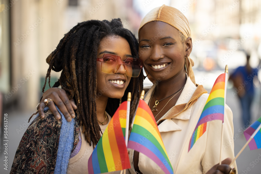 LGBTQ same sex black women couple waving rainbow flags on a city street ...