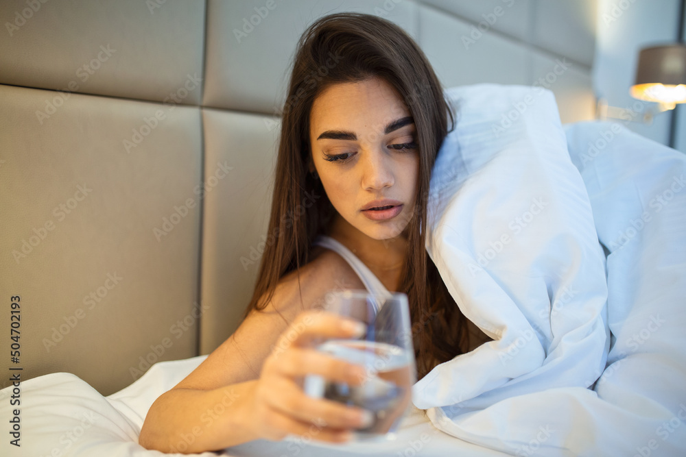 Young woman drinking glass of water in bed at night. Woman drinking a ...