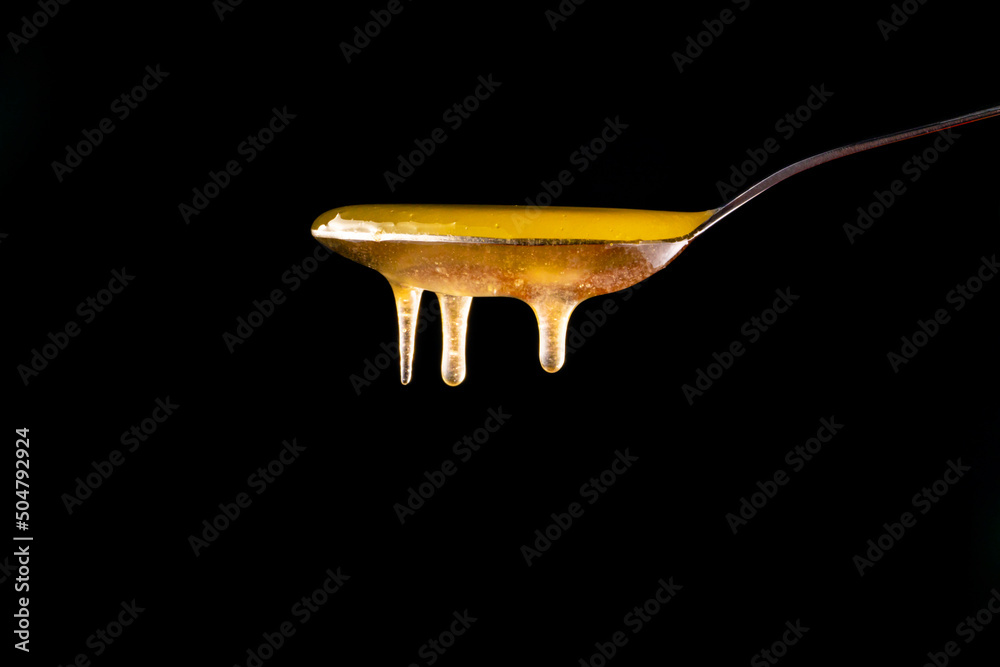 Honey dripping, pouring from spoon on a black isolated background ...