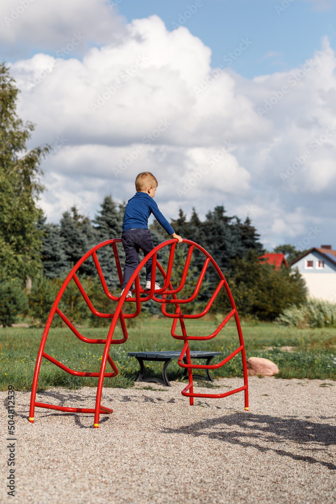 A little very brave boy climbs a metal, big red arched ladder on the ...