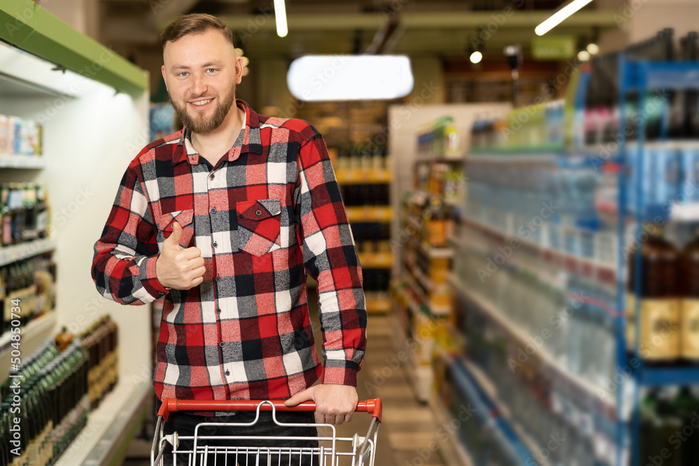 Handsome man shopping in a supermarket, push cart in a grocery store ...