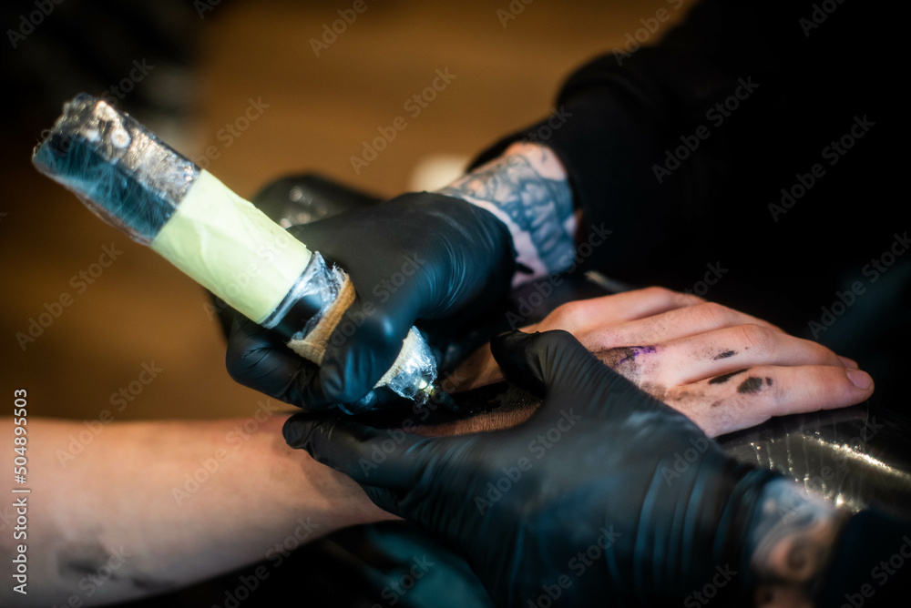 cropped shot of tattooing process on hand in salon. A professional ...