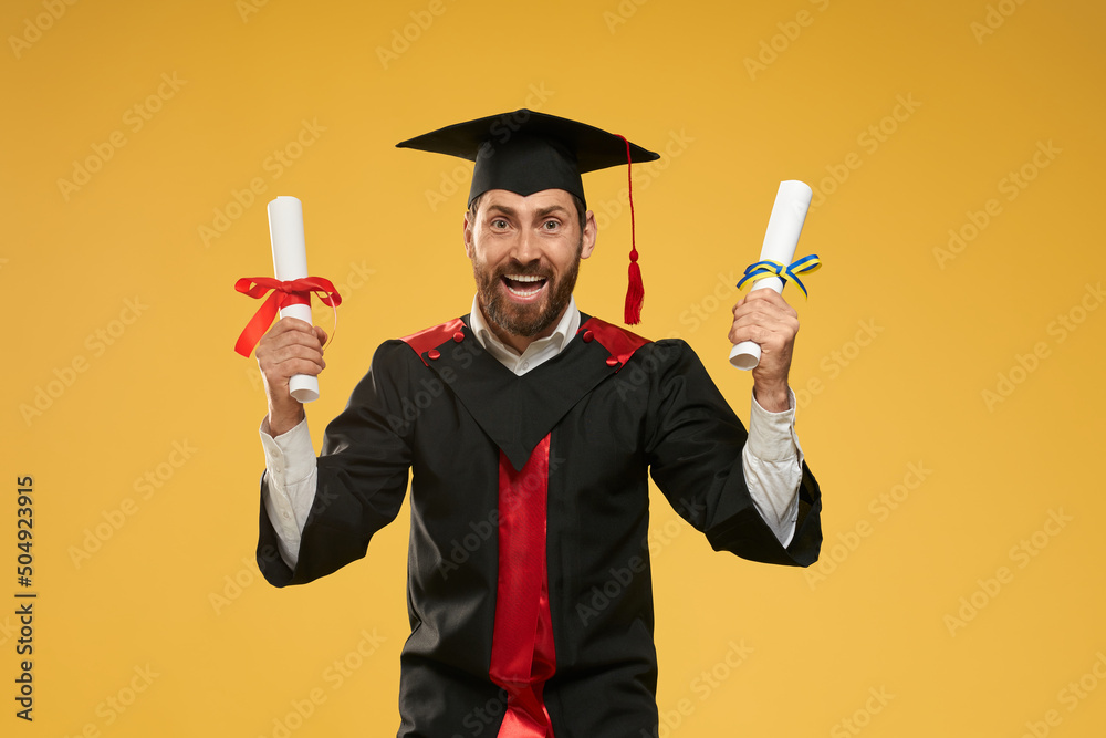 Front view of man wearing mortarboard and graduate gown standing with ...