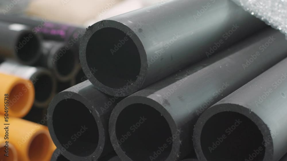 Stack of black plastic PE pipes in focus, yellow plastic pipes in ...