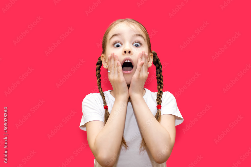 A child girl with pigtails on a red background with a surprised look ...