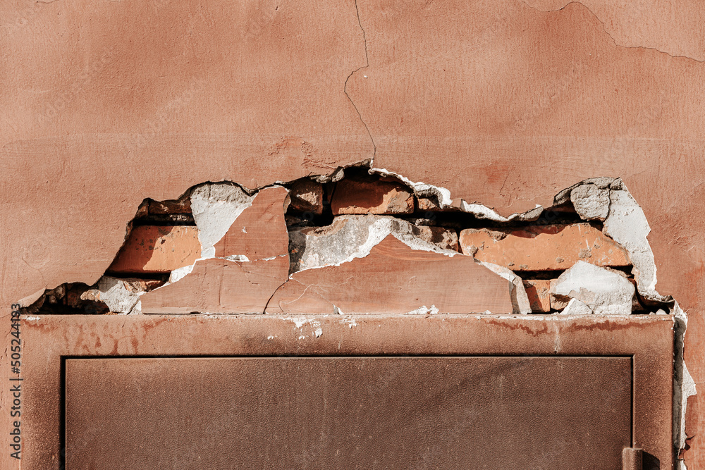 The destroyed wall of the building above the metal door. The plaster ...