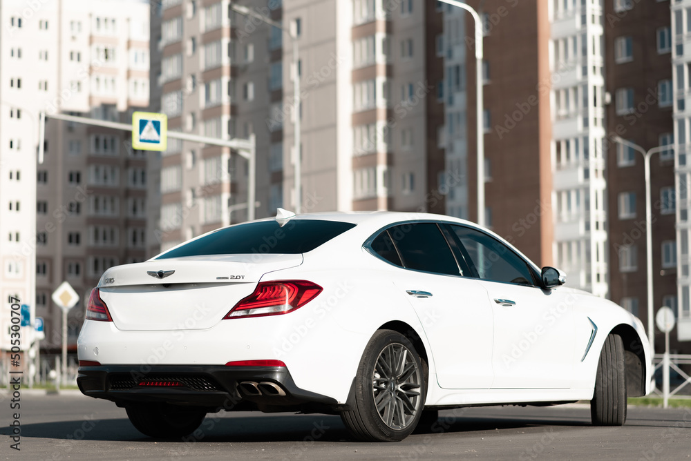 White Genesis G70 against the backdrop of high-rise buildings. Rear ...