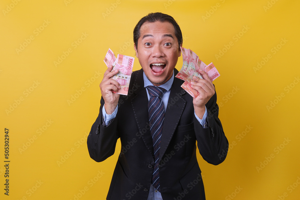 Attractive Asian man in business suit standing against yellow ...