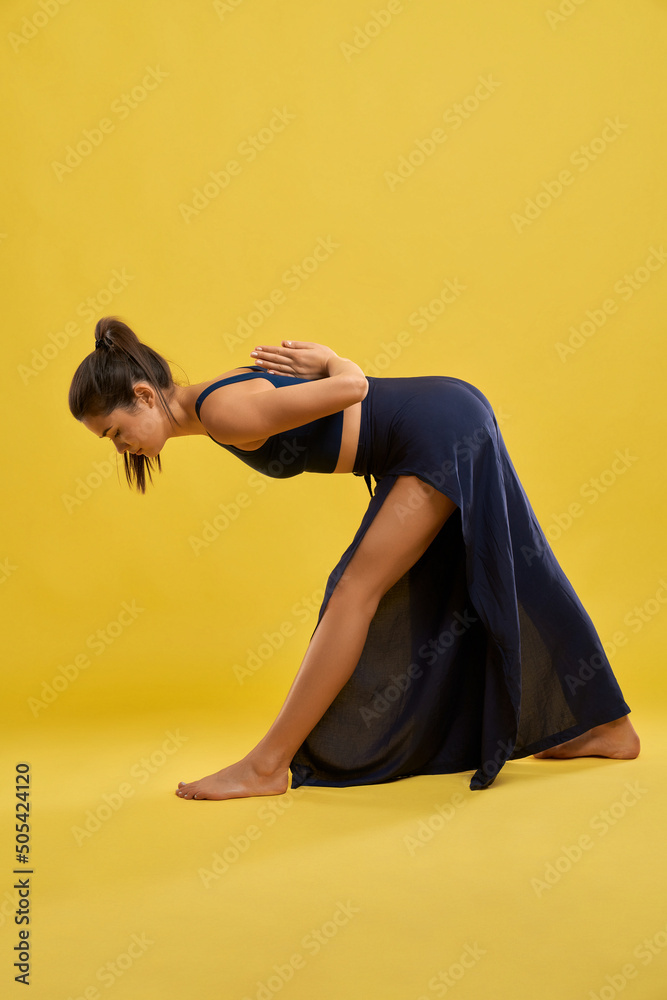 Slim woman bending forward, keeping hands behind back, while doing yoga ...