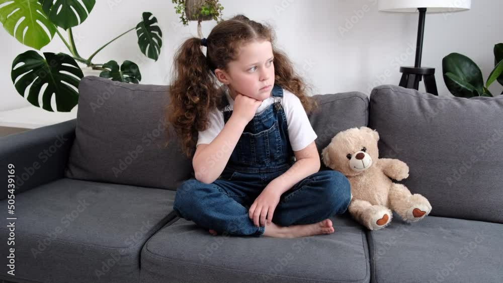Sad lonely kid sitting alone on grey couch in living room with teddy ...