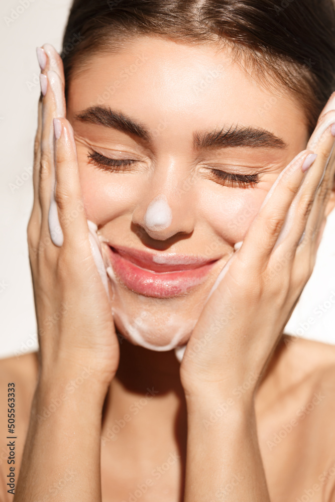 Cheerful female model applies foaming cleanser, has clean fresh healthy ...