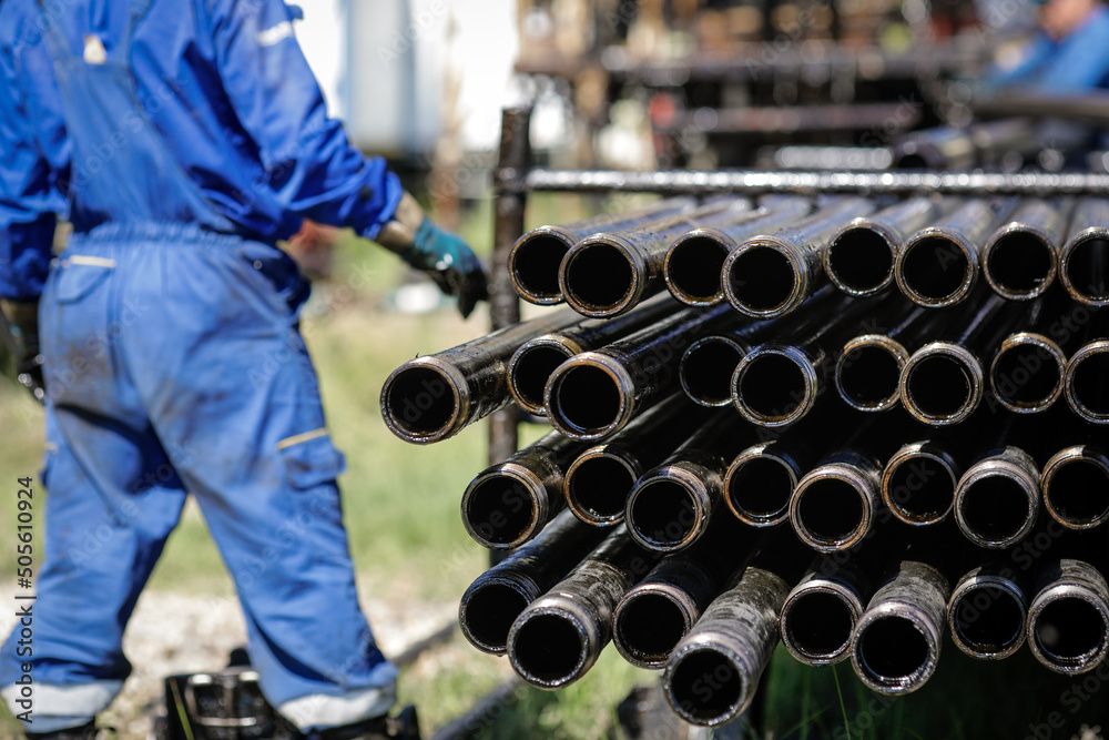 Oil rig drill pipes stacked with oil industry workers in the background ...