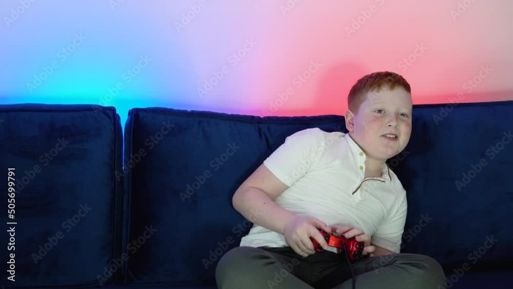 Excited little boy gamer is sitting on a couch, playing and winning in ...