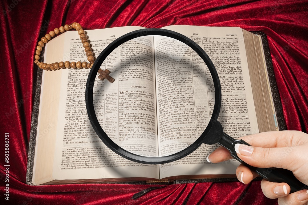 A magnifying glass in hand with open bible book. Stock Photo | Adobe Stock