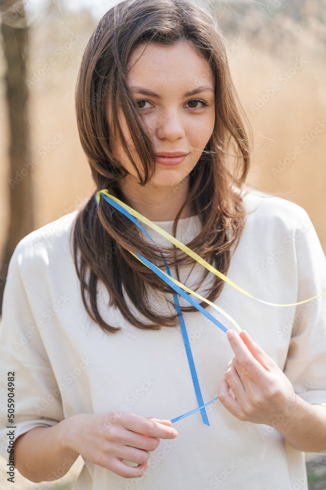 Smiling lady with blue and yellow ribbons in hair standing in nature ...