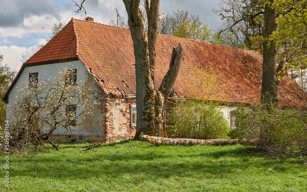 An old stone house. Red tile roof, wooden details. Green garden. Spring ...