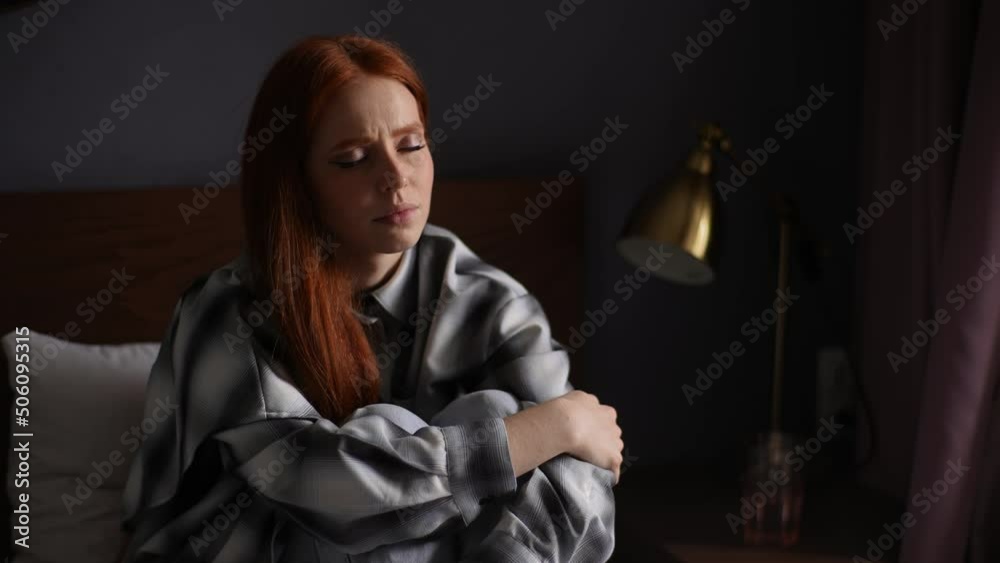 Depressed young woman sitting alone on bed with hugging knees and ...