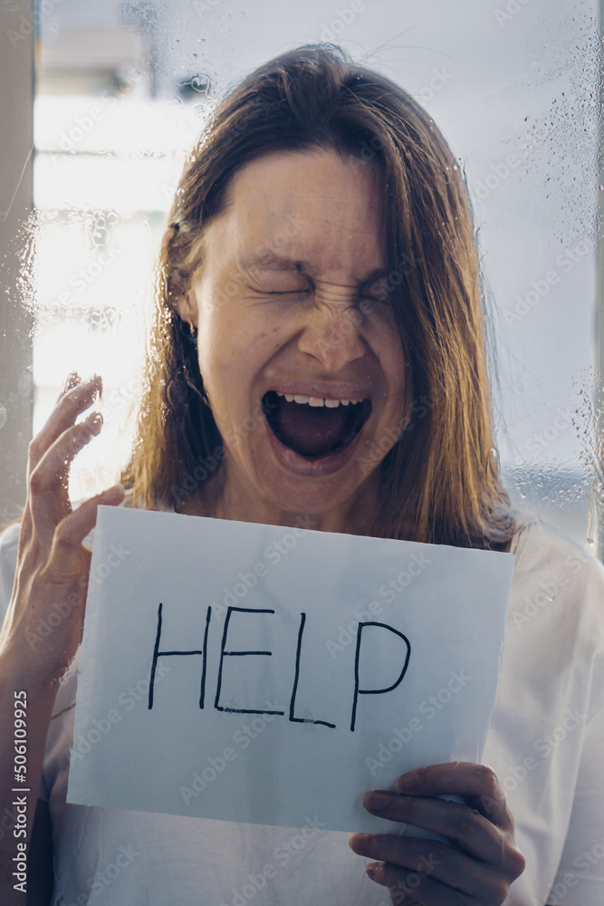 Young girl is crying and screaming behind wet glass, holding a sign ...
