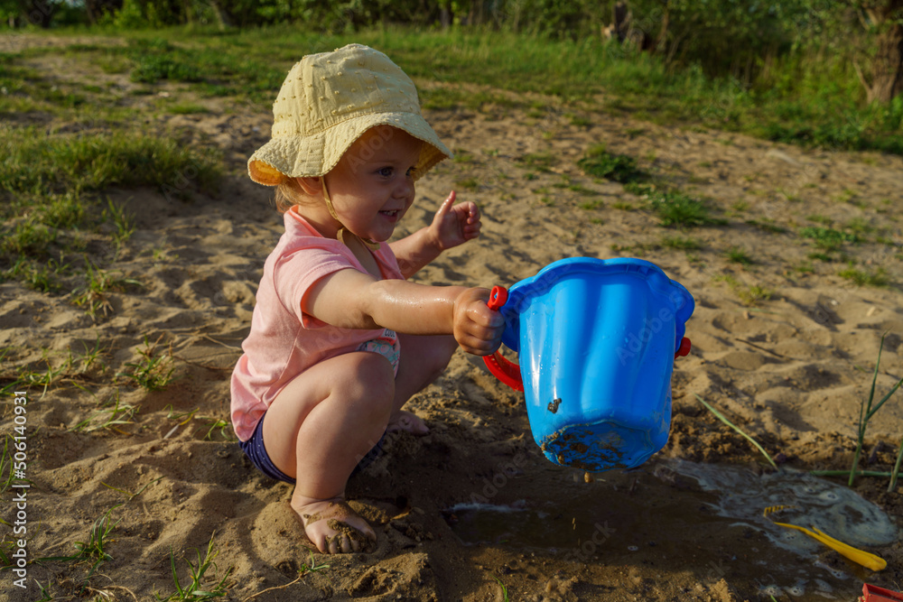 little baby playing with a blue plastic bucket filled with water on a ...