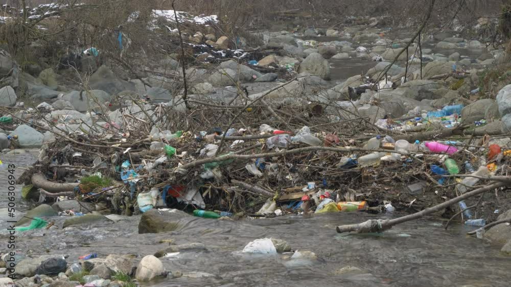 STATIC SHOT: Flowing river surrounded with a mix of debris and plastic ...