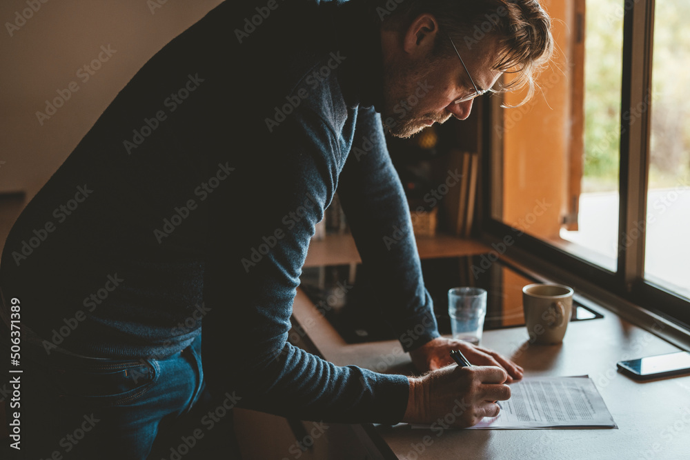 Mature man leaning on kitchen counter examining document at home Stock ...