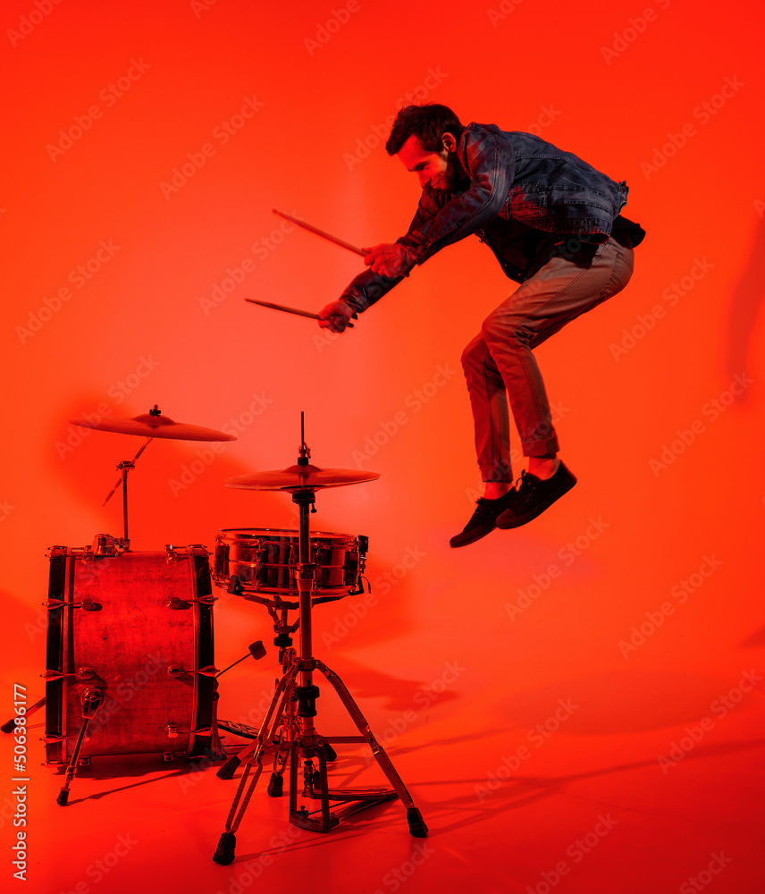 Young drummer jumps on his drums and holds drumsticks in his hands on a ...