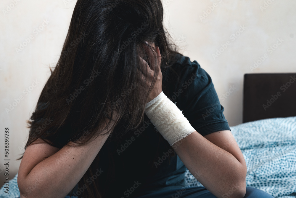 Young unhappy woman with a bandage on her hand hides her face ...