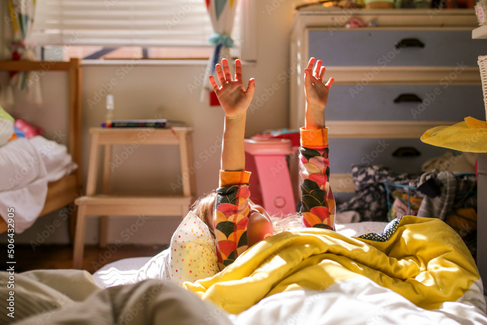 Girl in bed waking up in morning sunlight putting her arms up Stock ...