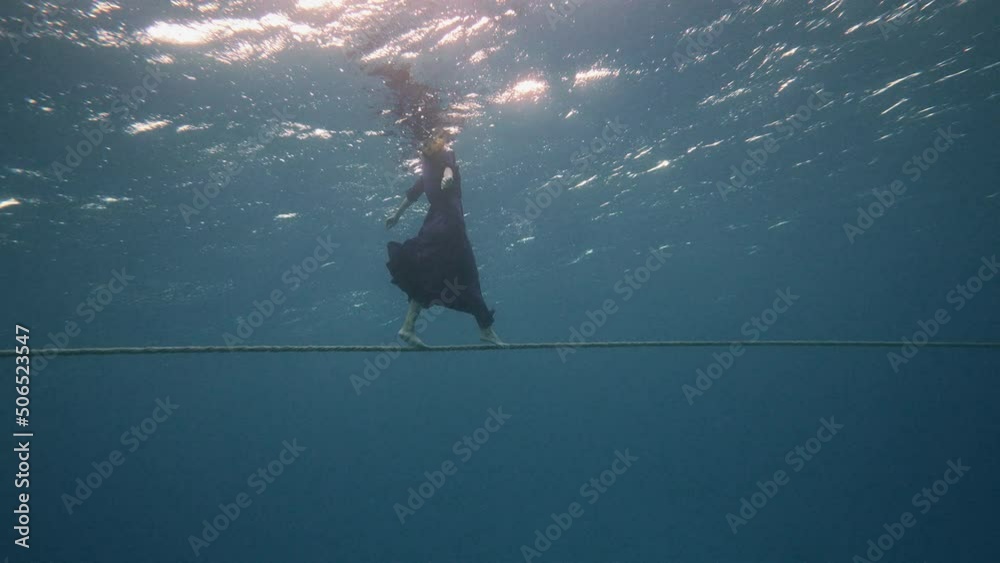 beautiful woman in flowing dress walk rope underwater dark background ...