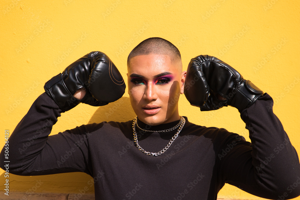 Young non-binary person wears boxing gloves on a mustard yellow ...