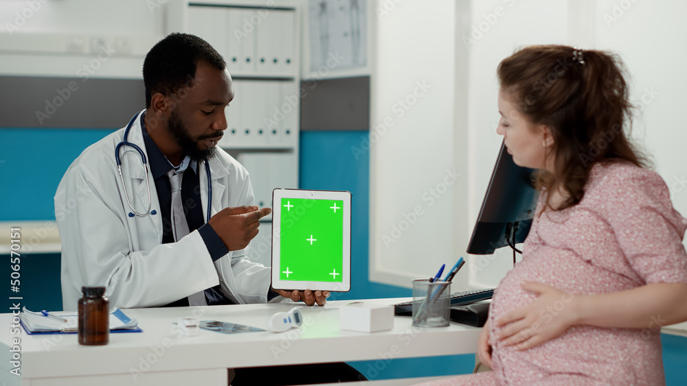 Pregnant woman and specialist looking at greenscreen on digital tablet ...