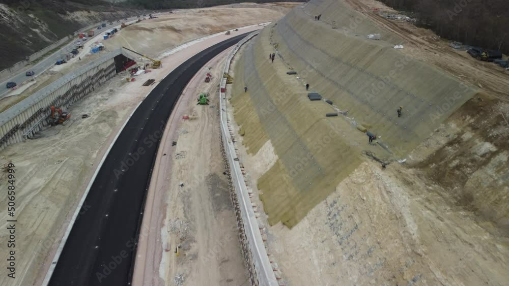 Workers reinforce the slope over the new road. Road construction in ...