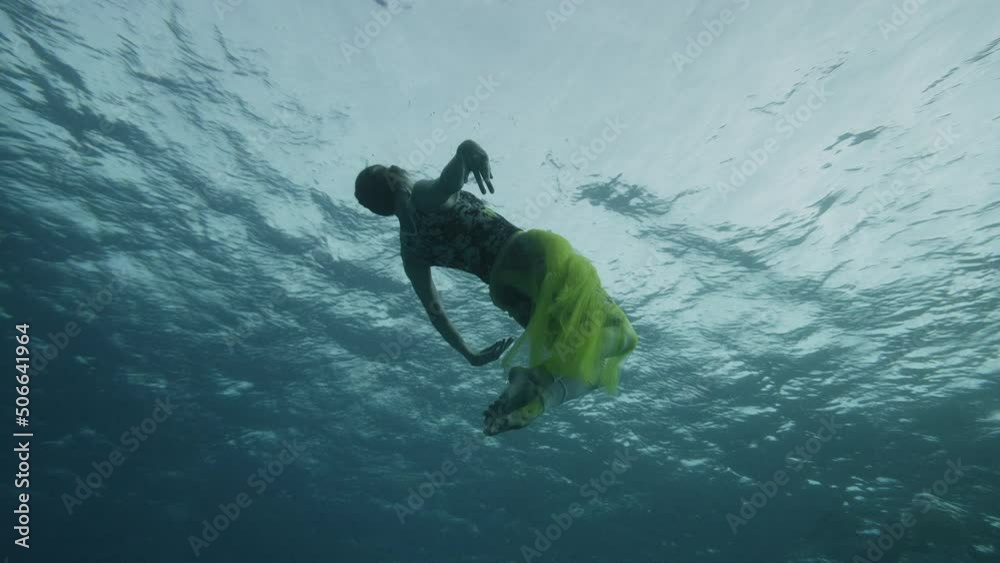 beautiful woman in flowing dress floats underwater dark background, she ...