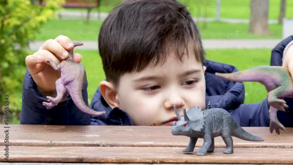 cute kid is playing with dinosaurs toys on park bench, spring, green ...