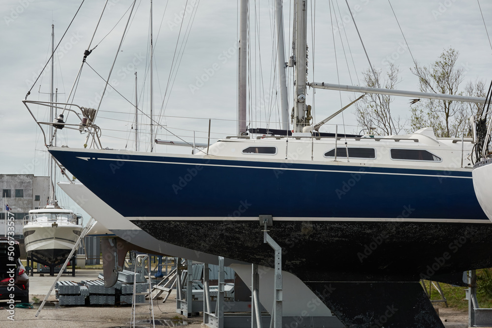 Blue sloop rigged sailboat standing on land in a yacht club. Service ...