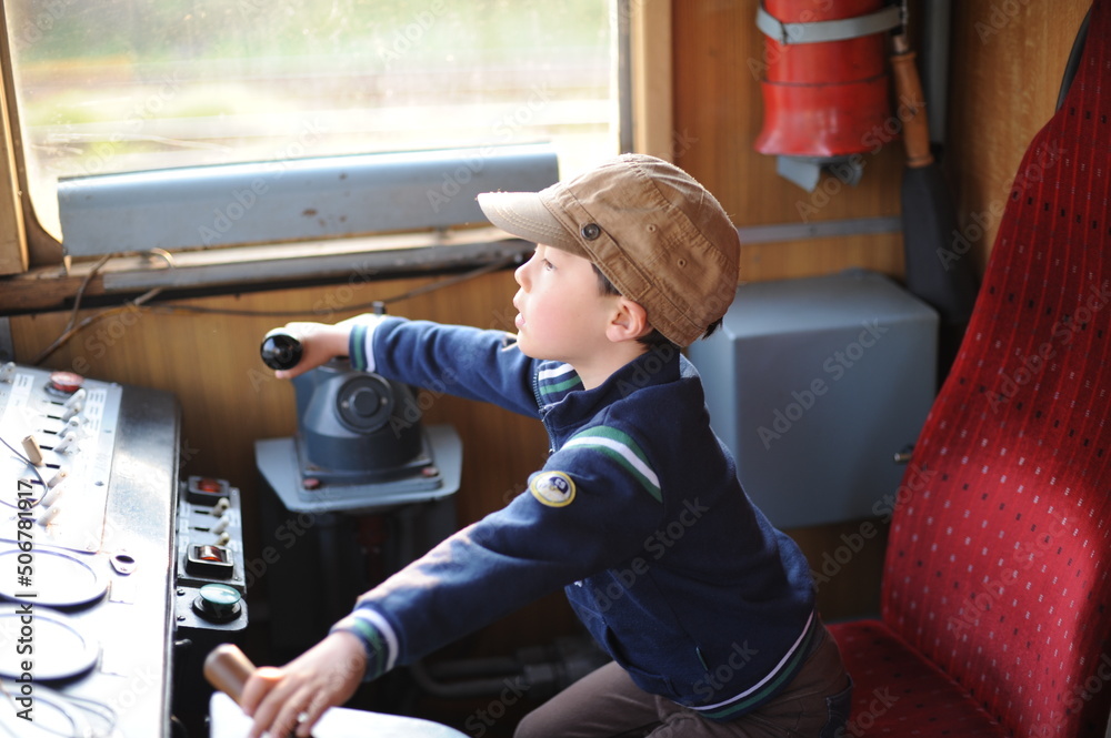 A young boy steering a locomotive and train in a driving compartment or ...