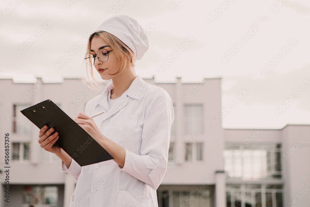 Young female nurse standing outside hospital infirmary writing patient ...