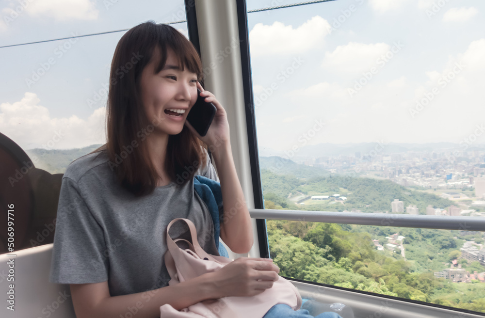 Smiling young Asian woman talking on mobile phone in gondola cable car ...
