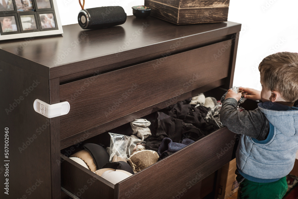 A small child opens a chest of drawers with clothes and goes through ...