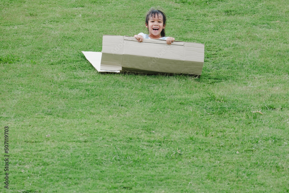 Smiling little girl sits on a cardboard box sliding down a hill at a ...